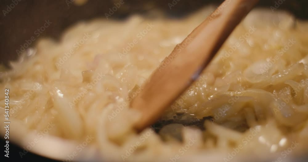 Onion cooking on butter in a pan wooden spoon stirs food in close up ...