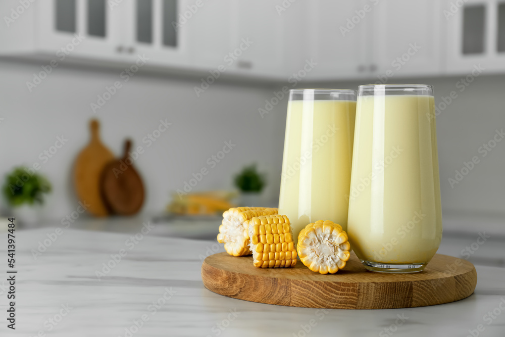 Tasty fresh corn milk in glasses and cobs on white table indoors. Space ...