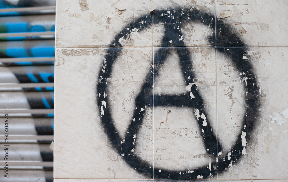 graffiti on the wall with a black anarchy symbol sign on a gray wall ...
