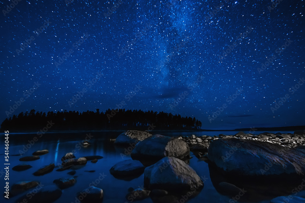 Foto de night landscape with a starry sky over sea water with stones ...