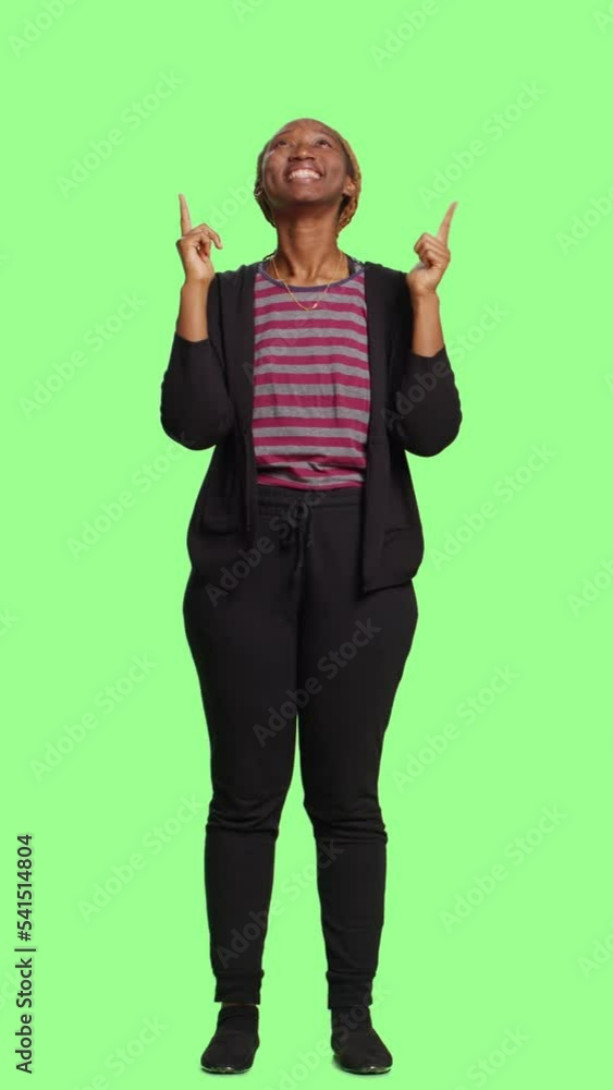 Vertical video: Optimistic woman pointing up with index fingers with ...