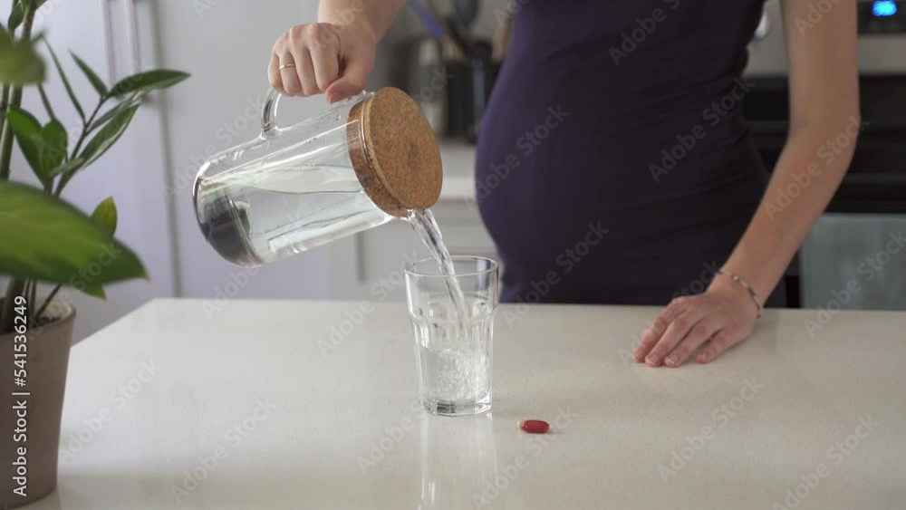 Pregnant women taking meds or vitamins in kitchen and drinking water ...