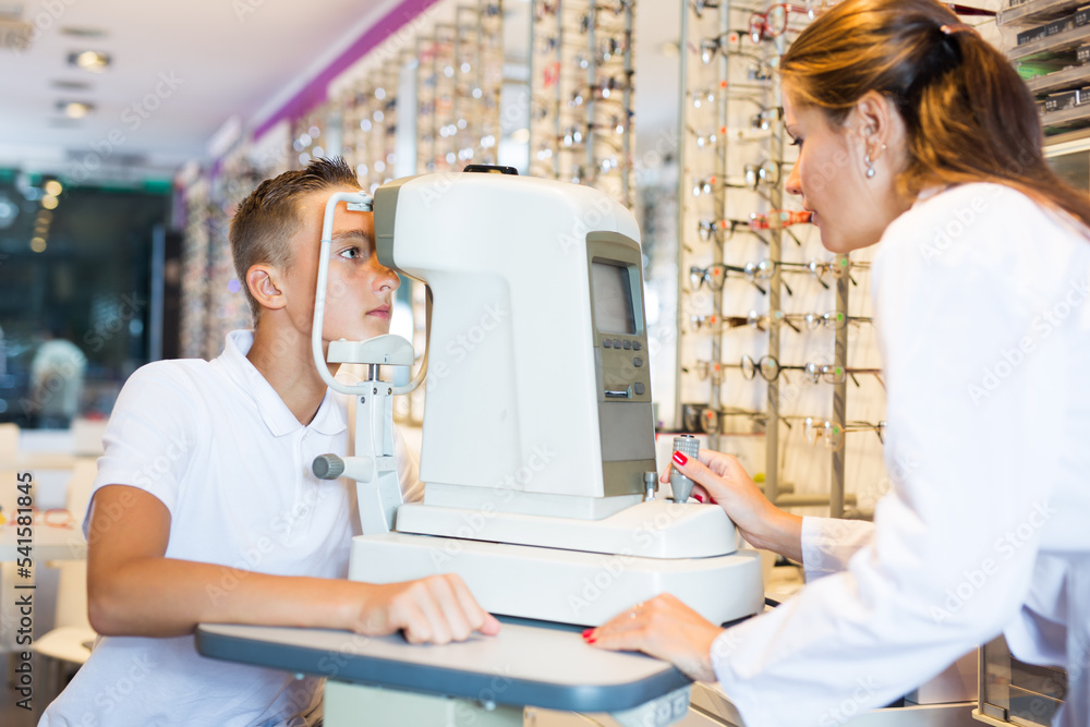 Qualified woman optometrist using refractometer for testing eyesight of ...
