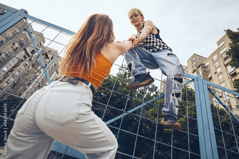 A teenage boy is helping his girlfriend climb up the railing in the ...
