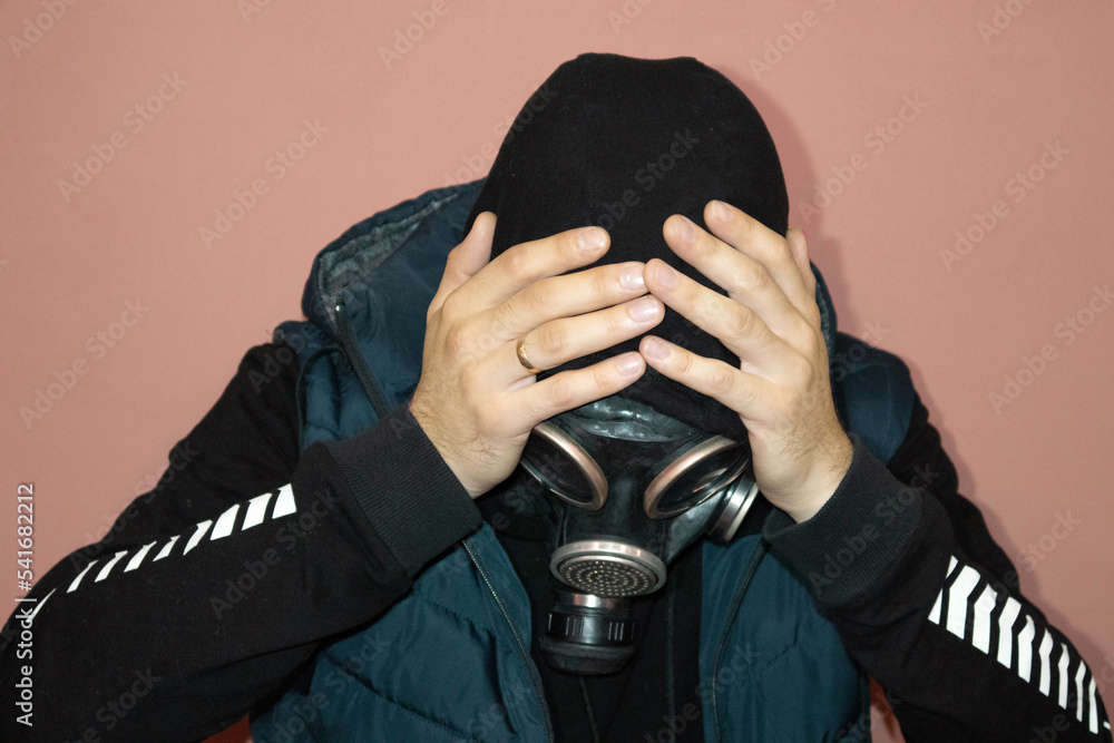A man wearing black clothing and a gas mask holds his hands over his ...
