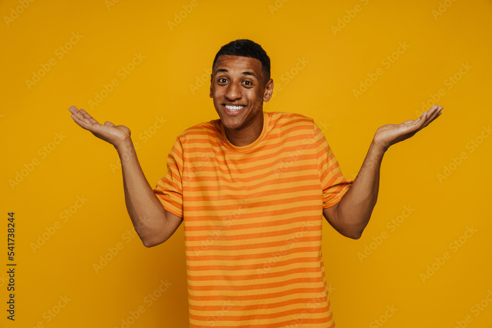 Smiling afro man shrugging shoulders and spreads hands sideways while ...
