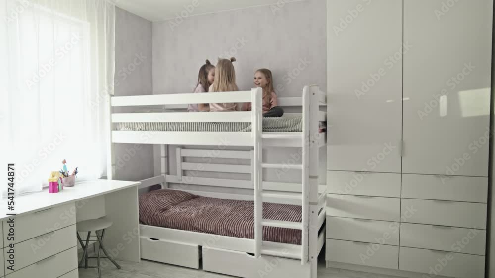 Three cute caucasian girls sit on second floor of a bunk bed in their ...