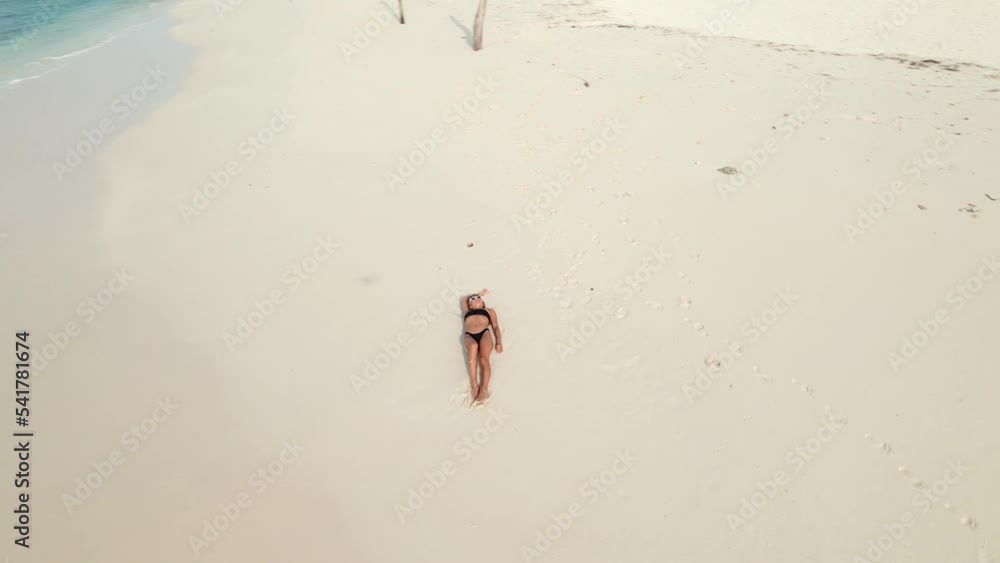 Drone flyover aerial shot of woman lying on sandy beach, ocean waves ...