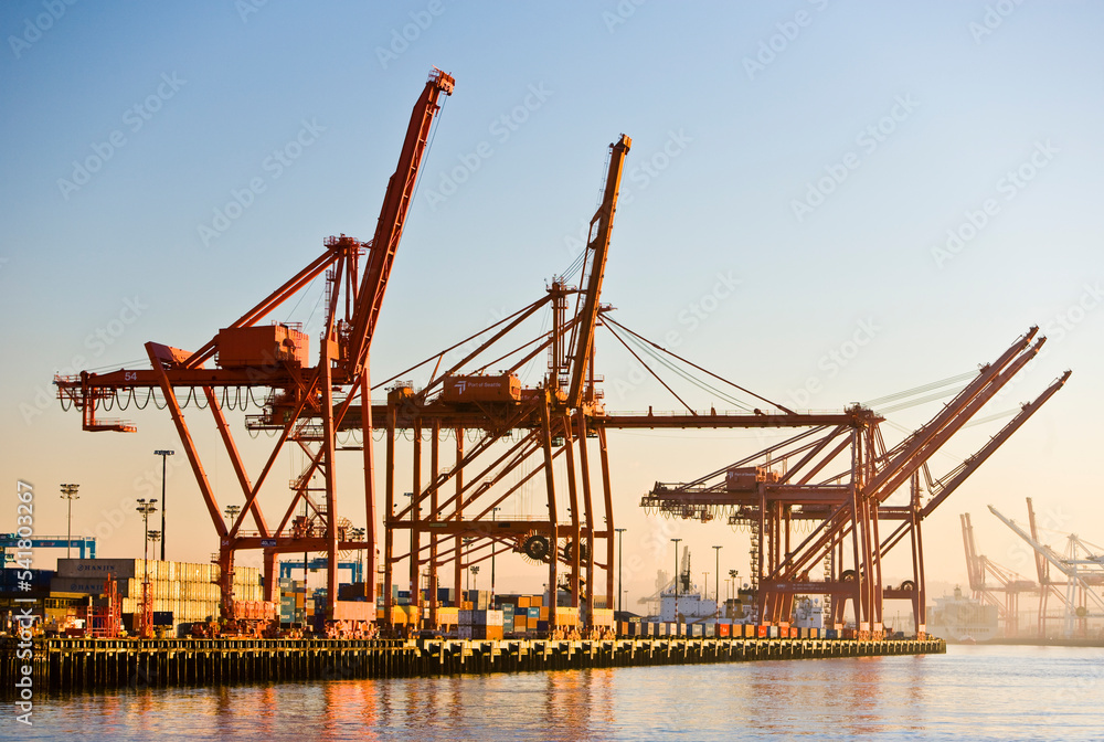 Cargo container cranes at a port wait for a ship to load at sunset ...