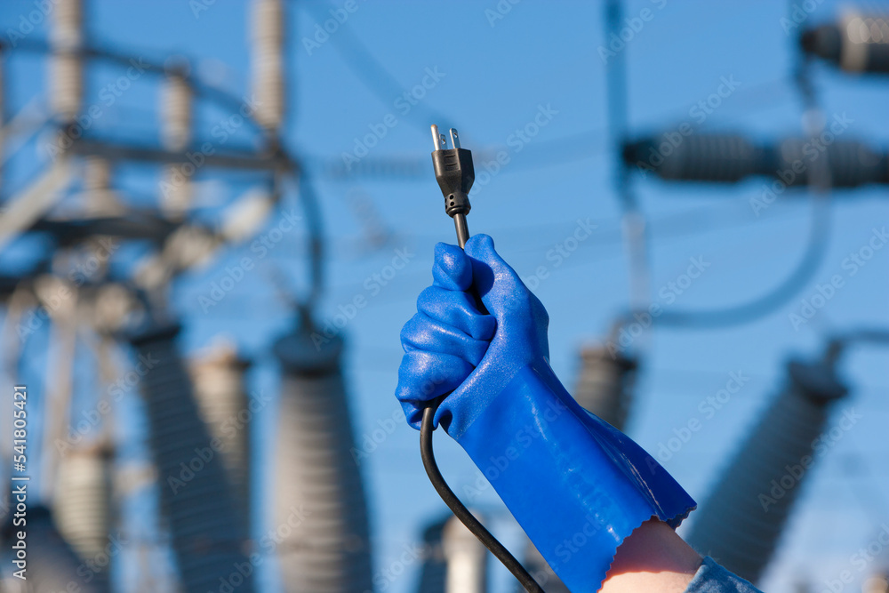 A gloved hand holds wires and plugs in front of an electrical utility ...