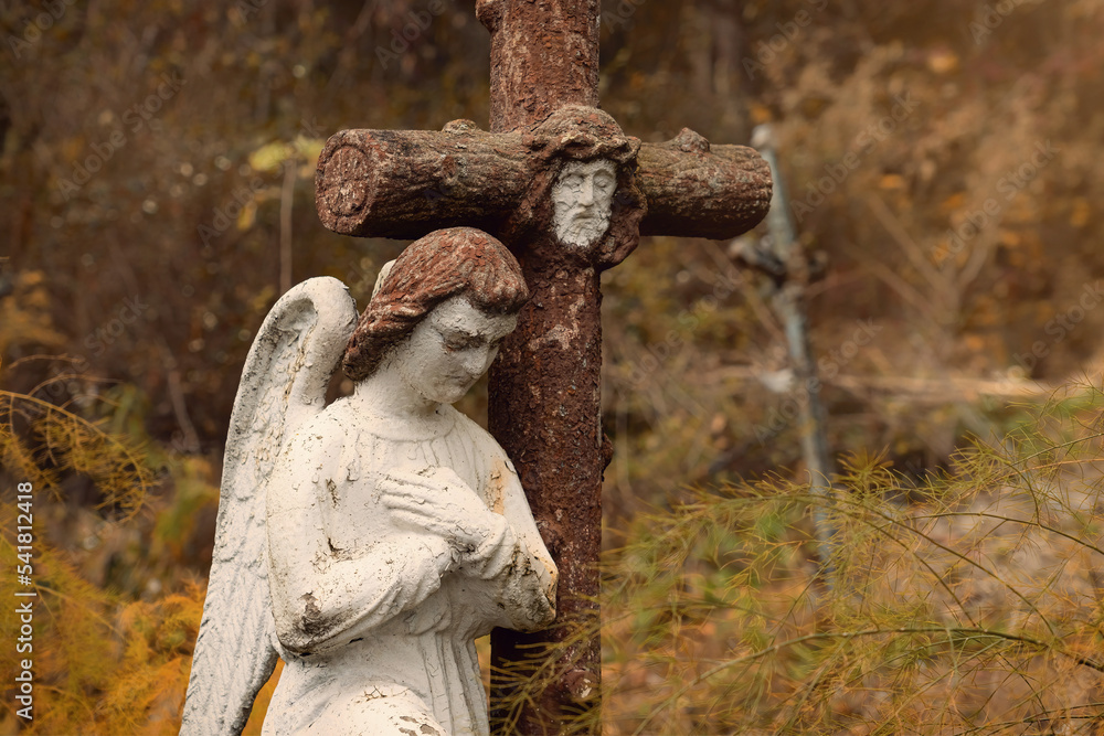 A white angel is praying. A statue stands next to an old cross (concept ...