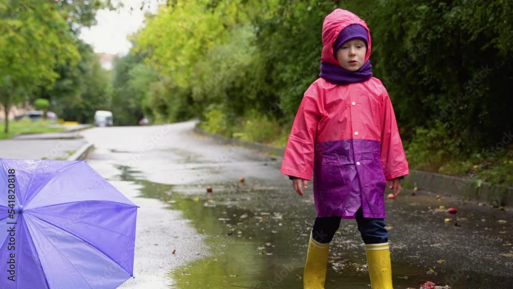 Children with umbrella and rain boots play outdoors in heavy rain. Kid ...