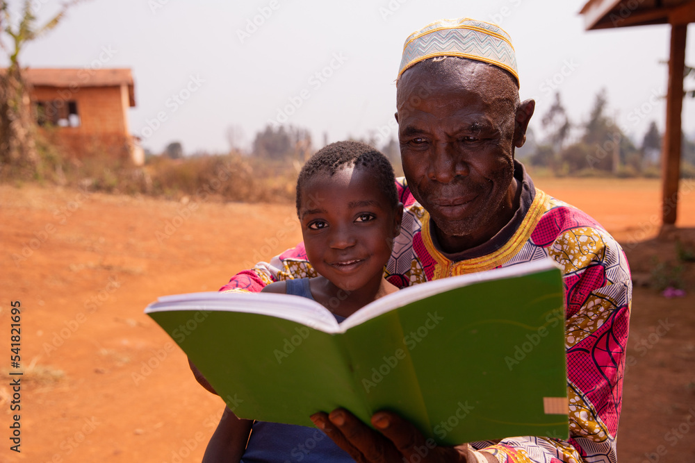 African grand father educating his grandson outdoor under the sun ...