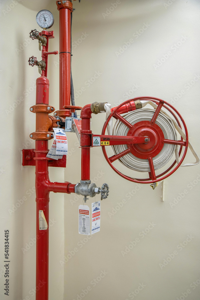 Red steel fire hose reel hooked up to red pipes and valves in a hallway ...
