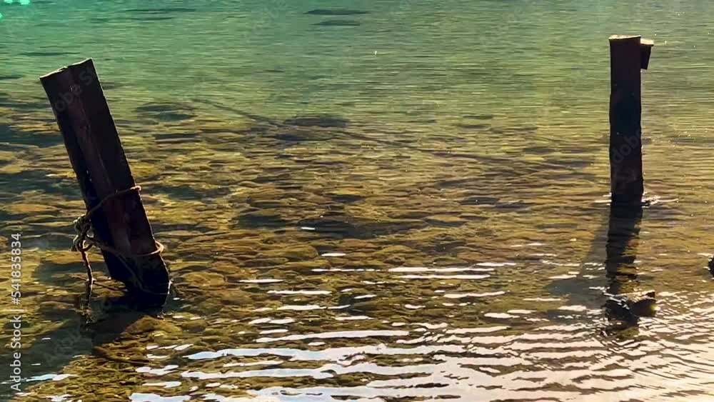 A close-up shot on two wooden posts stuck in a clear lake water ...