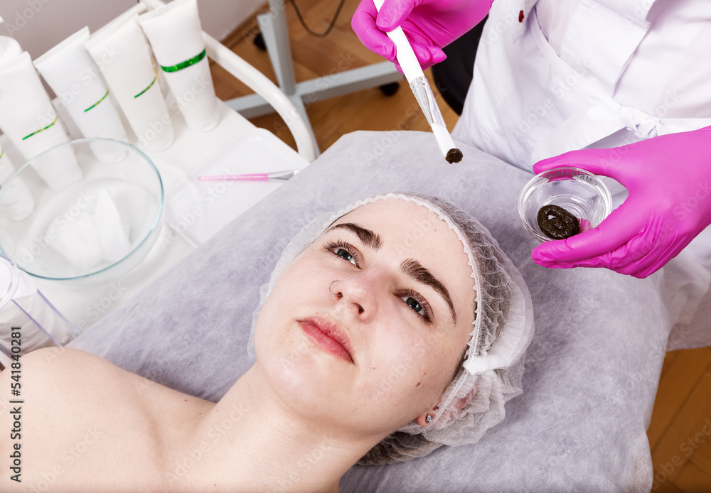 Cosmetologist preparing to apply a white cosmetic mask on the face of a ...