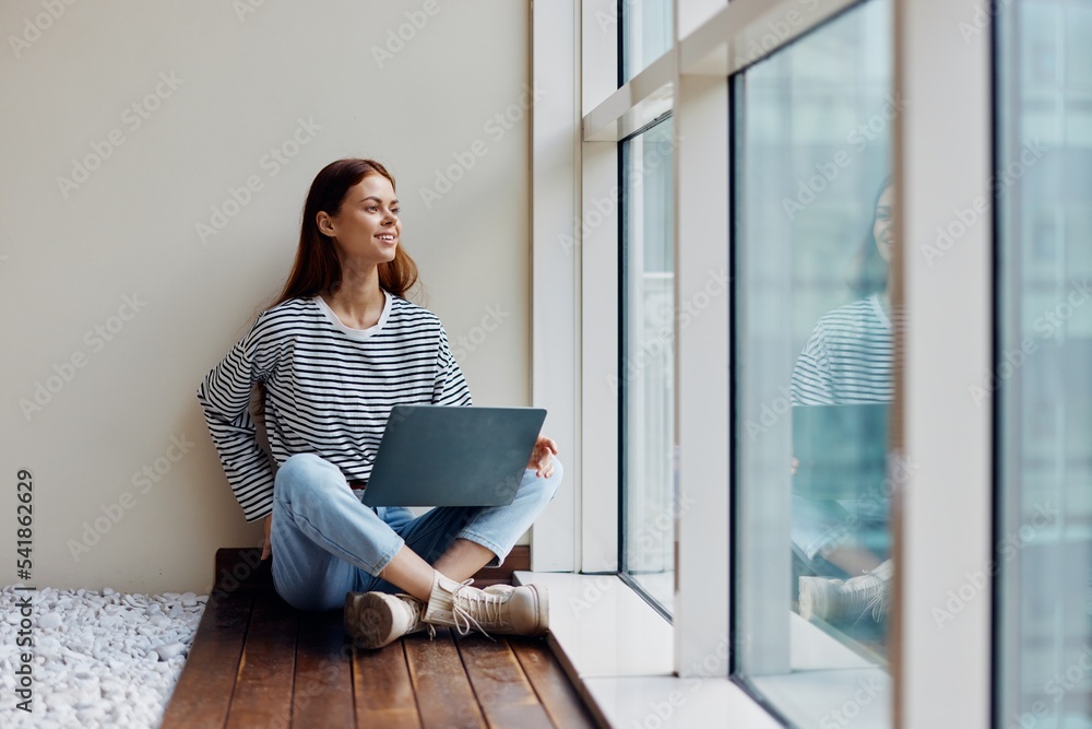 Business woman sitting with a laptop at the window full-length and ...