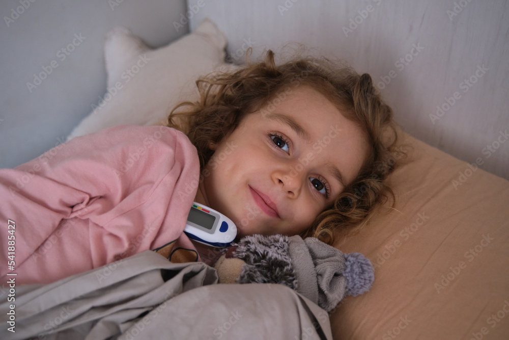 sick girl lying in bed with a fever is controlled with a thermometer ...