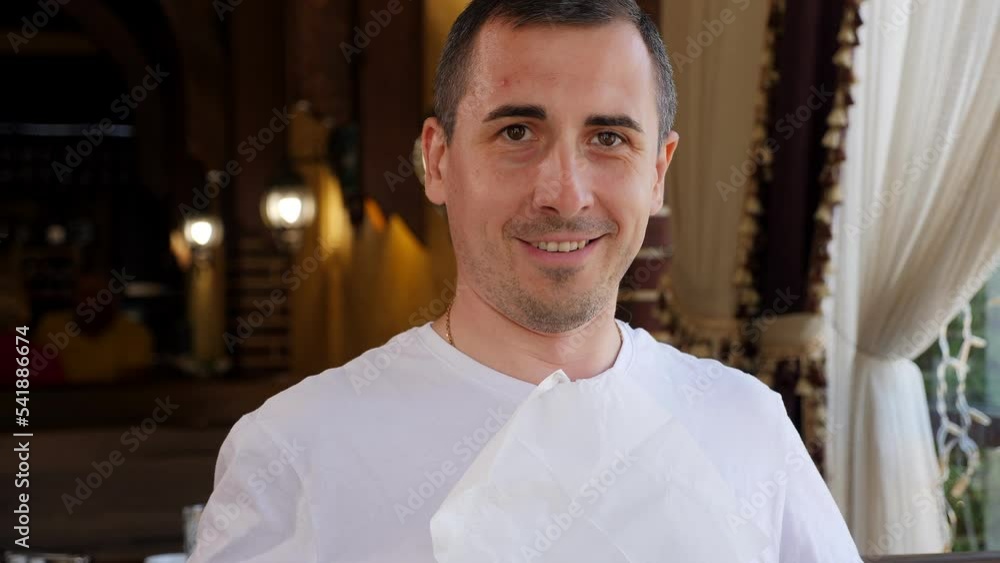 Portrait of a young man with a napkin at a cafe table, he puts a napkin ...