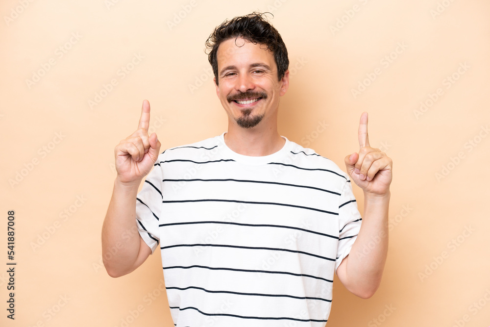 Young caucasian man isolated on beige background pointing up a great ...