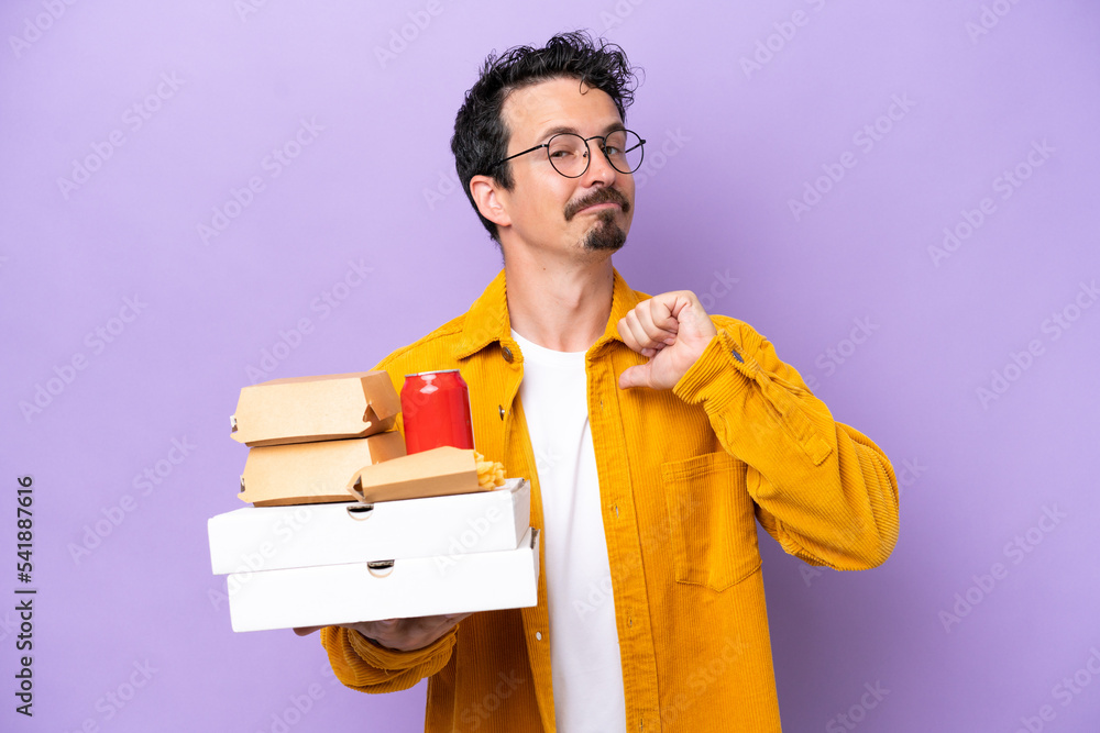 Young caucasian man holding fast food isolated on purple background ...