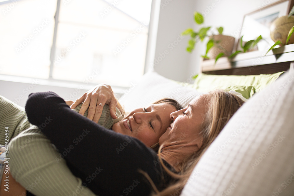 Two blonde women on the bed with white sheets cuddling and hugging ...