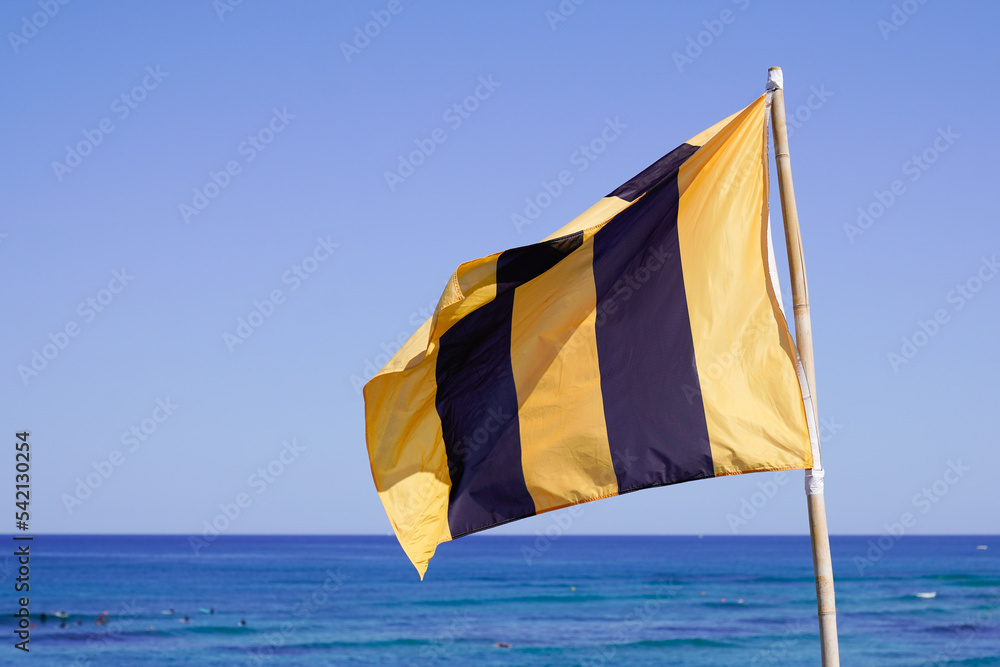 Warning flag yellow black vertical line blowing on the beach on sunny ...