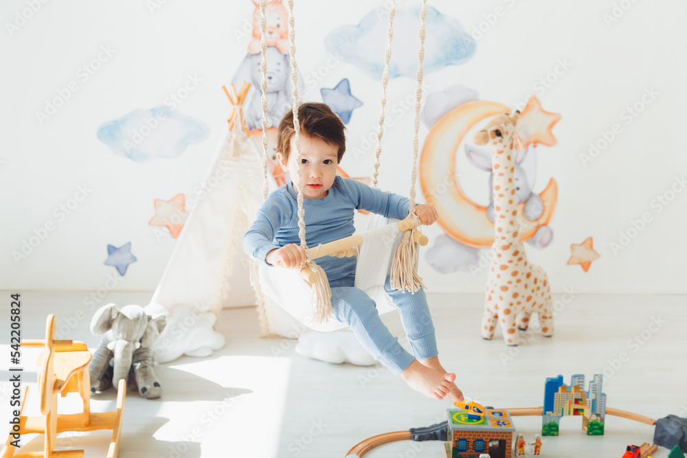 asian cute kid rides in a hanging swing in his room.Suspended home ...