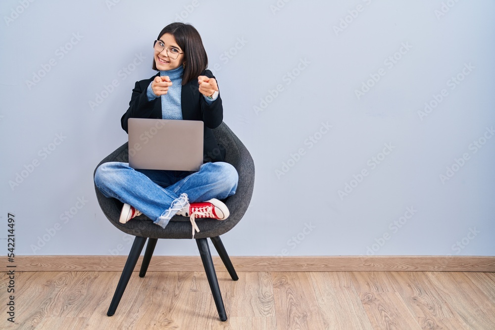 Young hispanic woman sitting on chair using computer laptop pointing ...