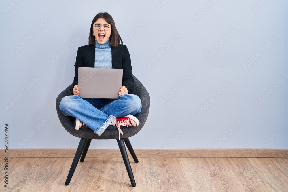 Young hispanic woman sitting on chair using computer laptop angry and ...