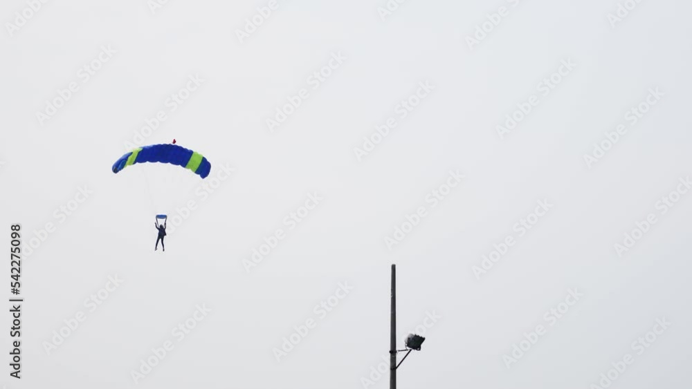 Skydiver slowly lands in a field. Parachutist with yellow and blue ...