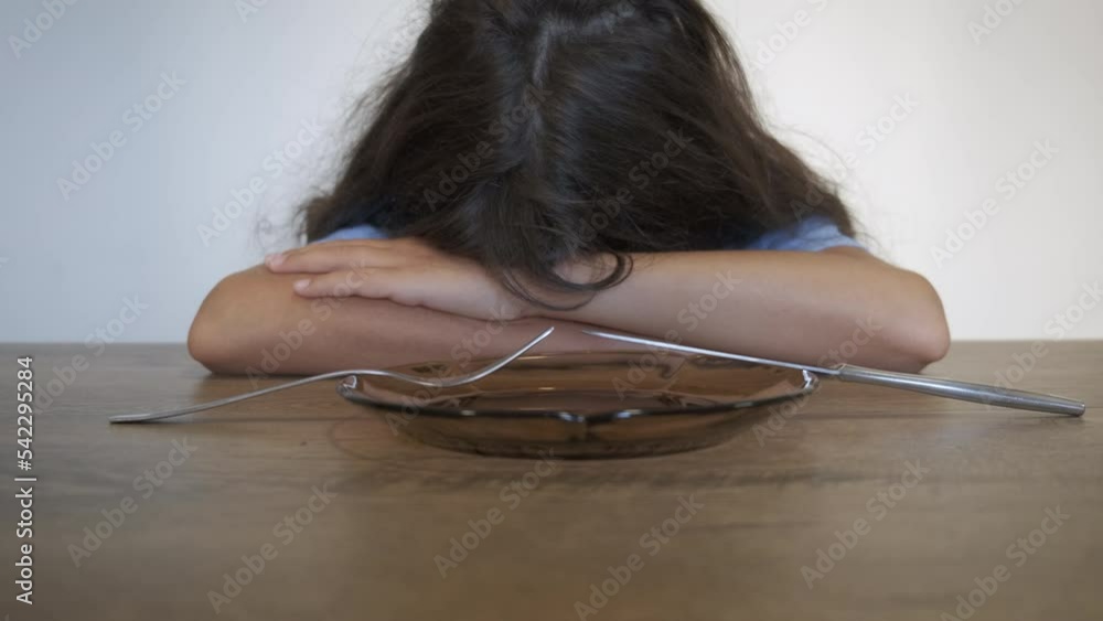 Empty plate during poverty. A poor hungry child sits by the table with ...
