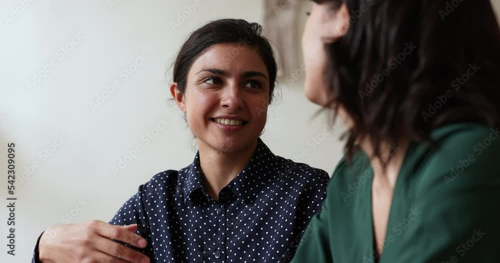 Attractive smiling Indian female talks to workmate seated at workplace ...