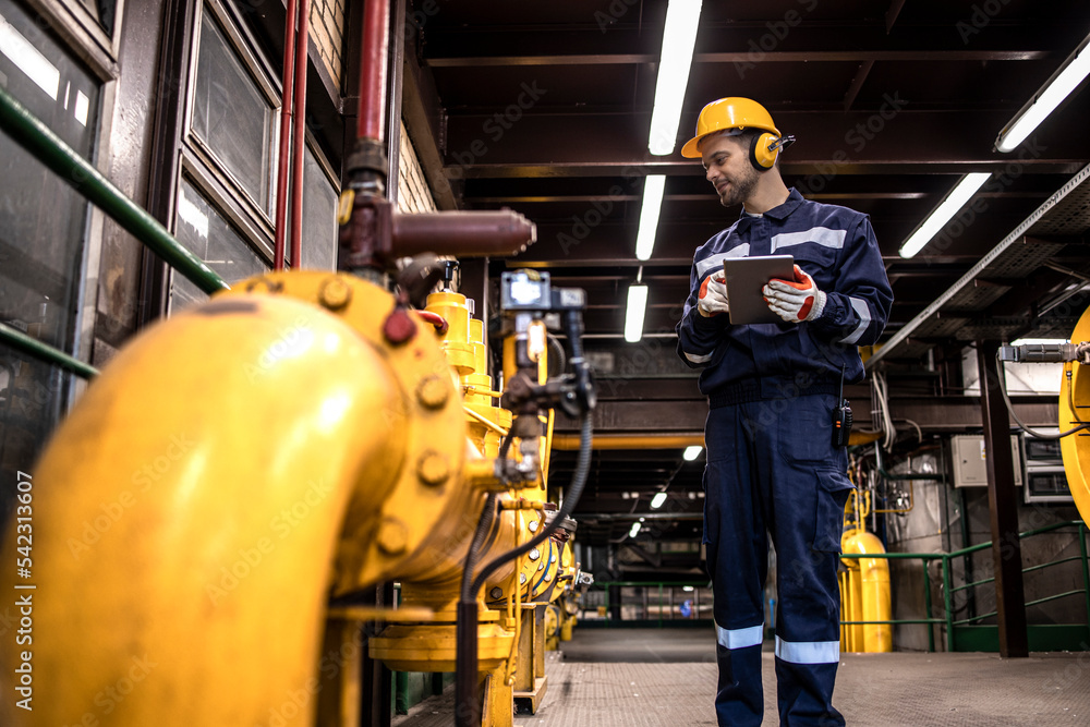 Gas refinery worker walking by pipes inside power plant and taking ...