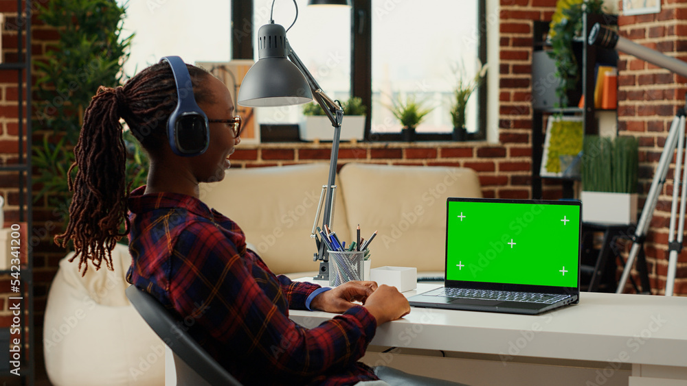 Office worker wearing headset and using laptop with greenscreen display ...