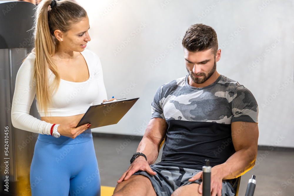 Muscular handsome man doing exercises on leg press machine and female ...