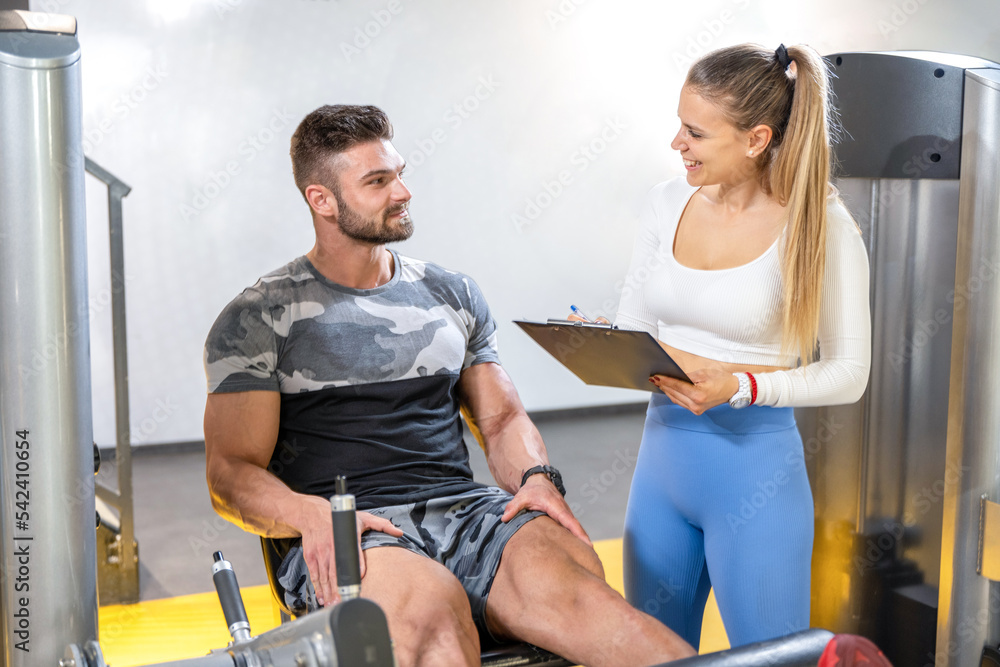 Muscular handsome man doing exercises on leg press machine and female ...