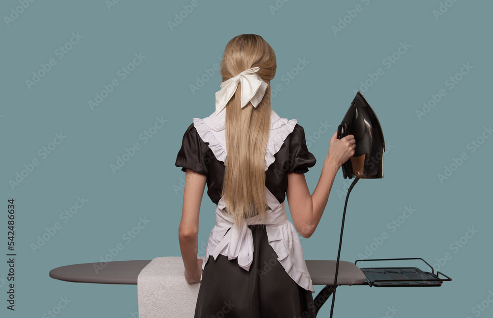 A woman dressed as a maid irons a towel on an ironing board. Back view ...