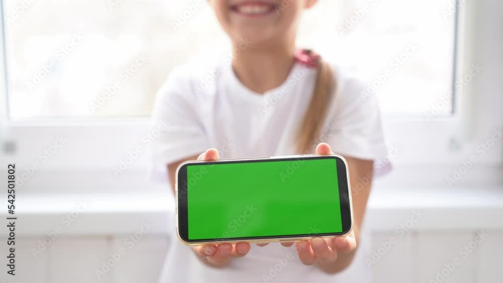 A little girl shows a smartphone horizontally with a chroma key ...