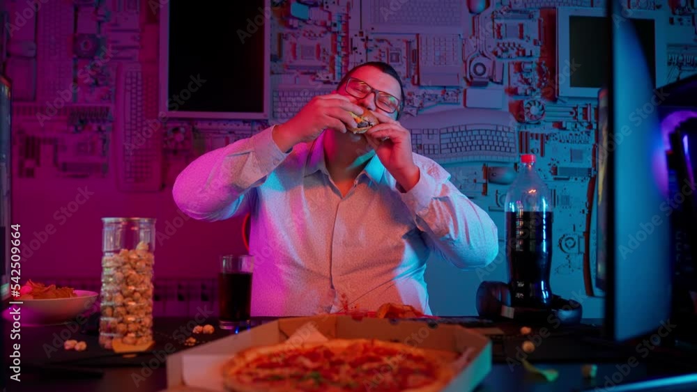 The gamer plays at the computer and eats a burger and pizza. A Thick ...