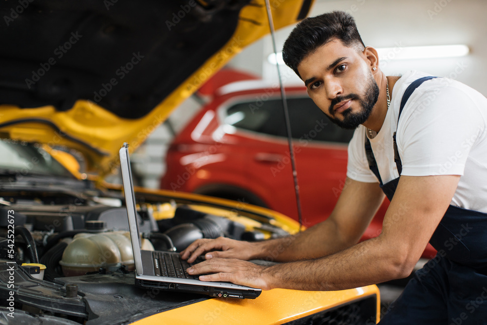 Young man car mechanic maintains vehicle using diagnostic laptop ...