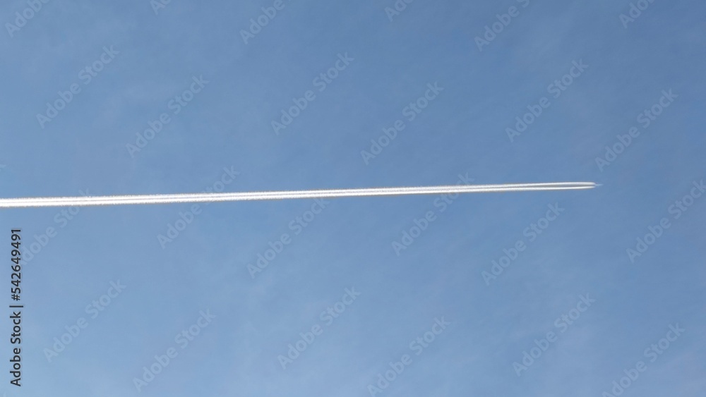 A long white trail from a flying plane. A jet plane flies in a light ...