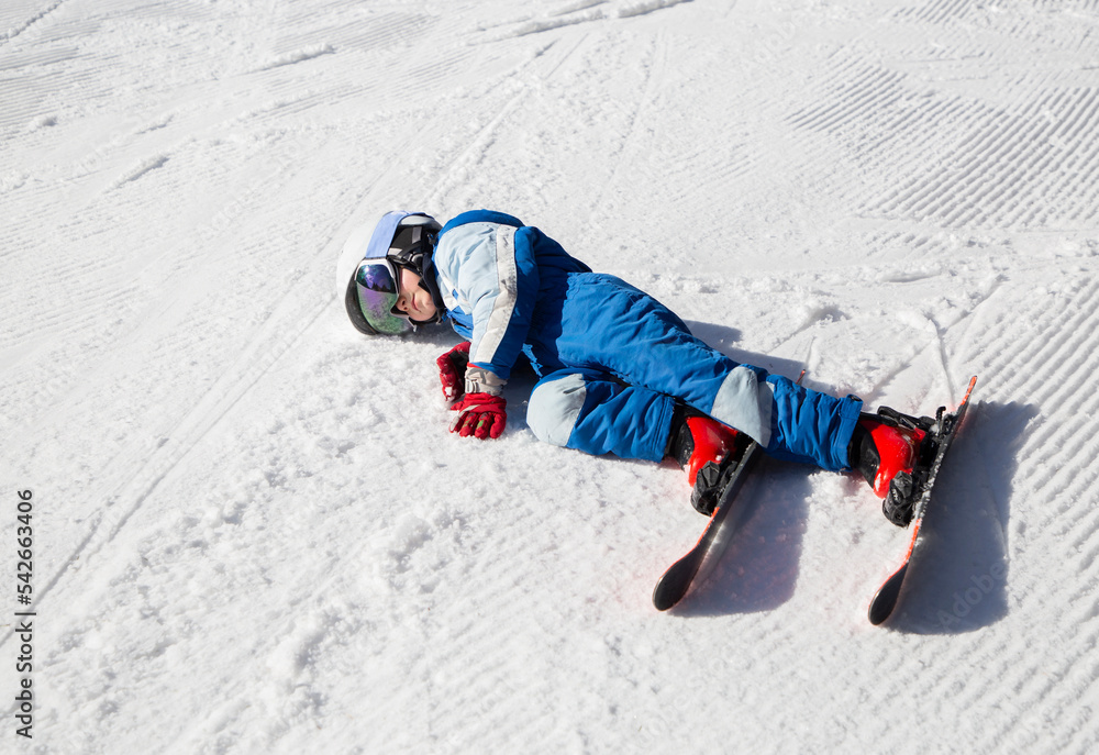 tired child in a helmet, glasses, skis and winter overalls lies on the ...