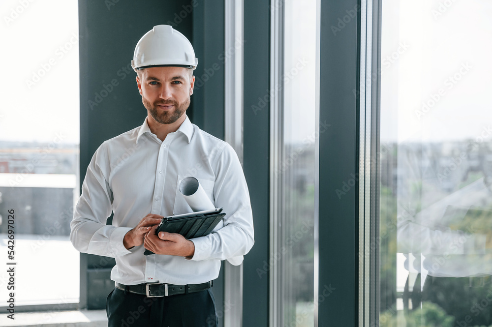 Standing near panoramic windows. Man in white shirt is working indoors ...