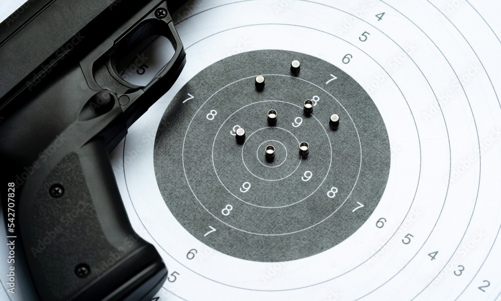 Black air gun pellet gun laying on a paper shooting target next to a ...