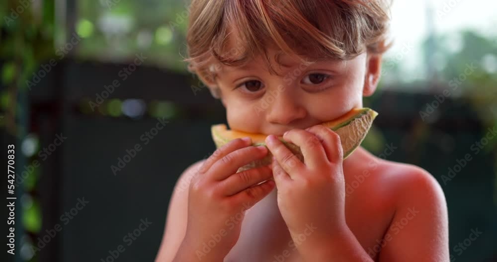Child taking a bite of yellow melon fruit. Shirtless little boy eating ...