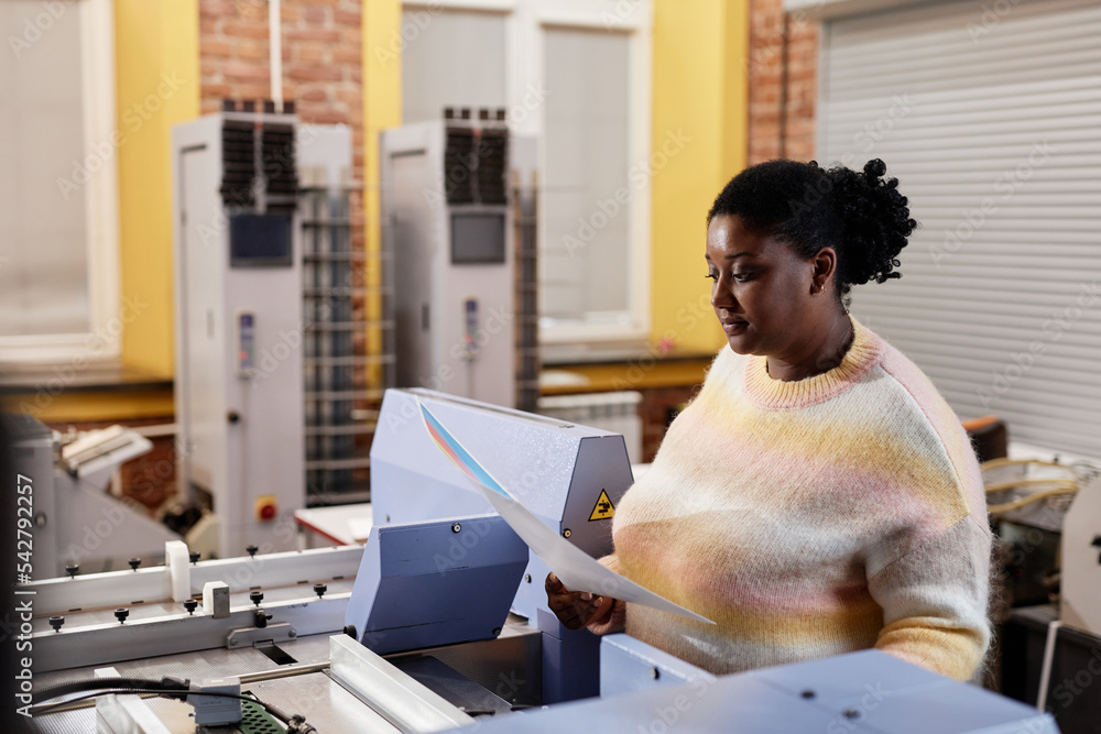 Side view portrait of young black woman operating printing machine and ...
