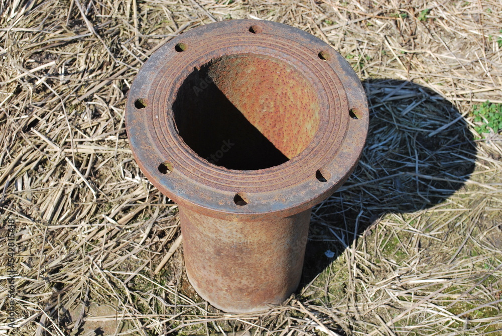 close-up on a metal pipe with a collar and holes, stuck vertically into ...
