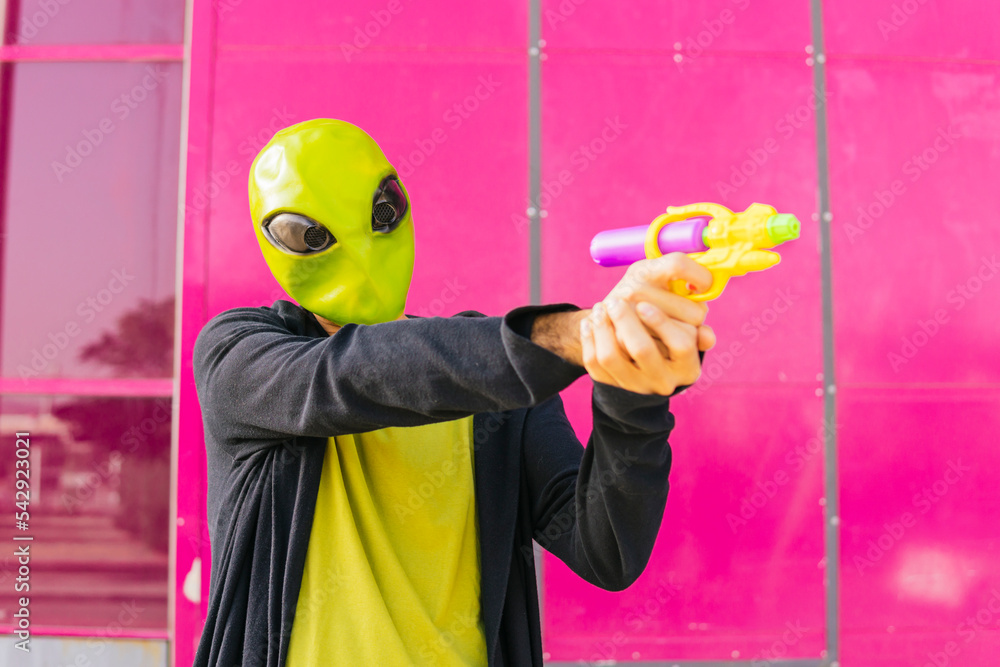 Man wearing alien mask playing with toy gun in front of pink wall Stock ...