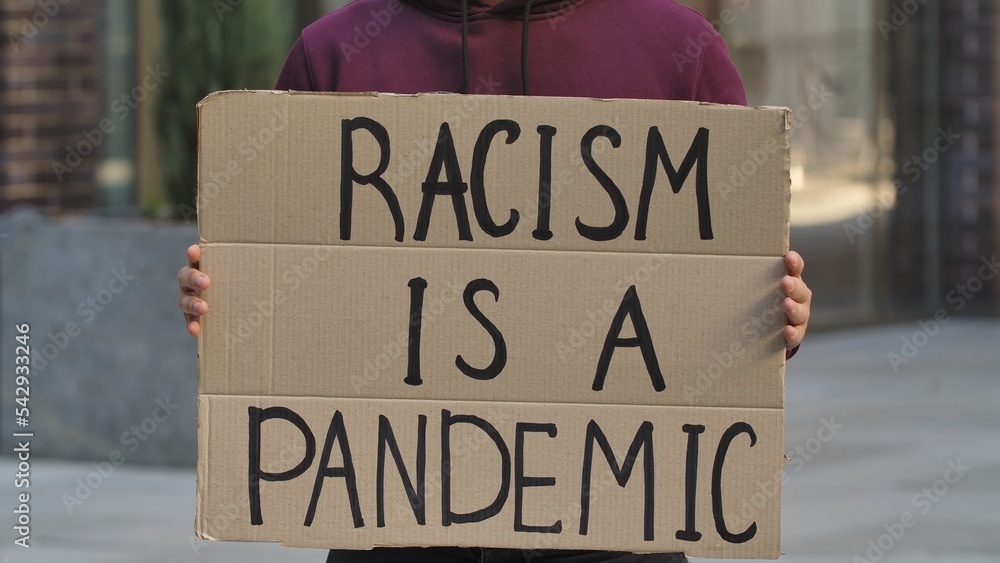 RACISM IS A PANDEMIC on cardboard poster in hands of male protester ...